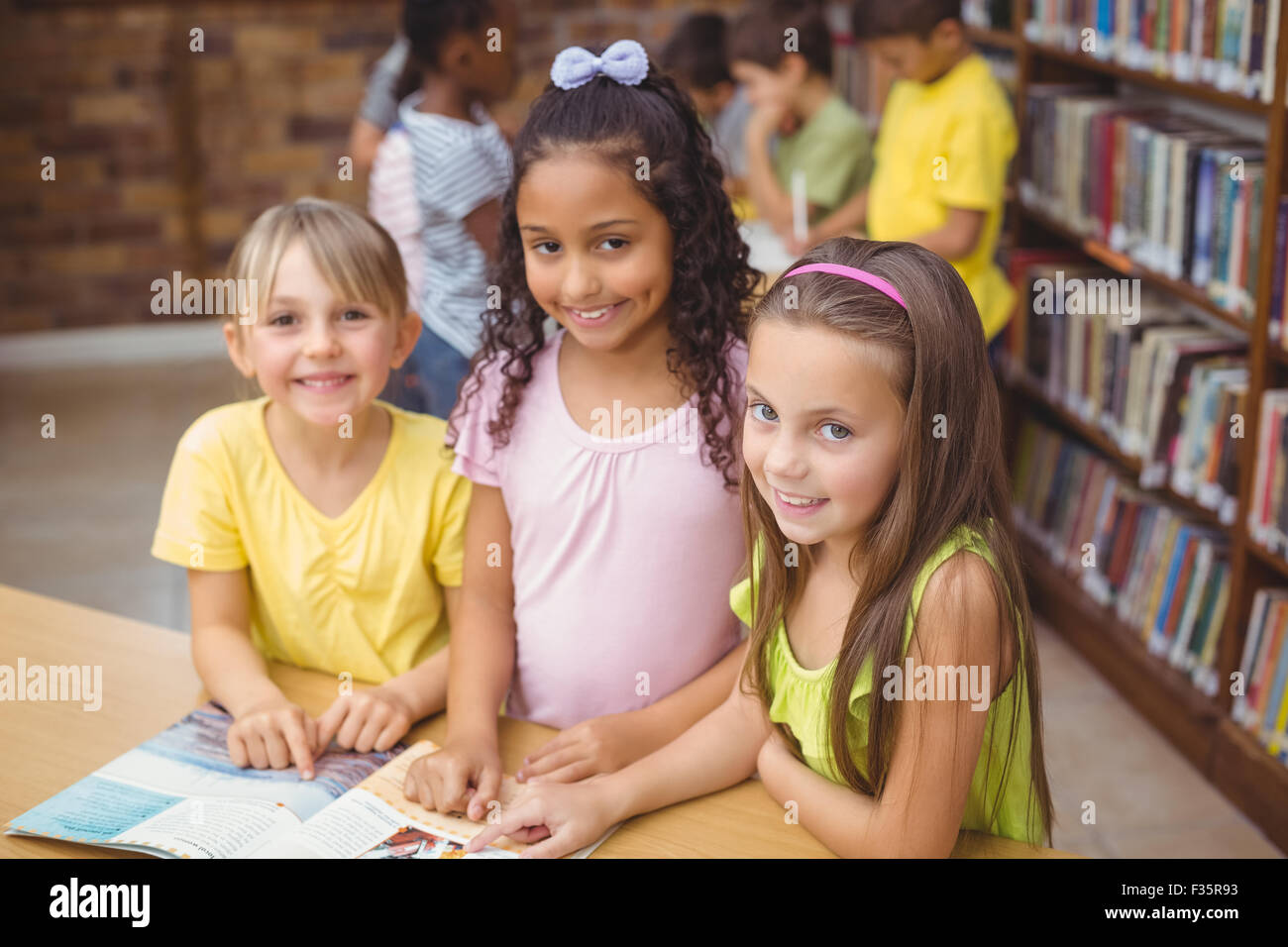 Pupils reading book together in library Stock Photo - Alamy