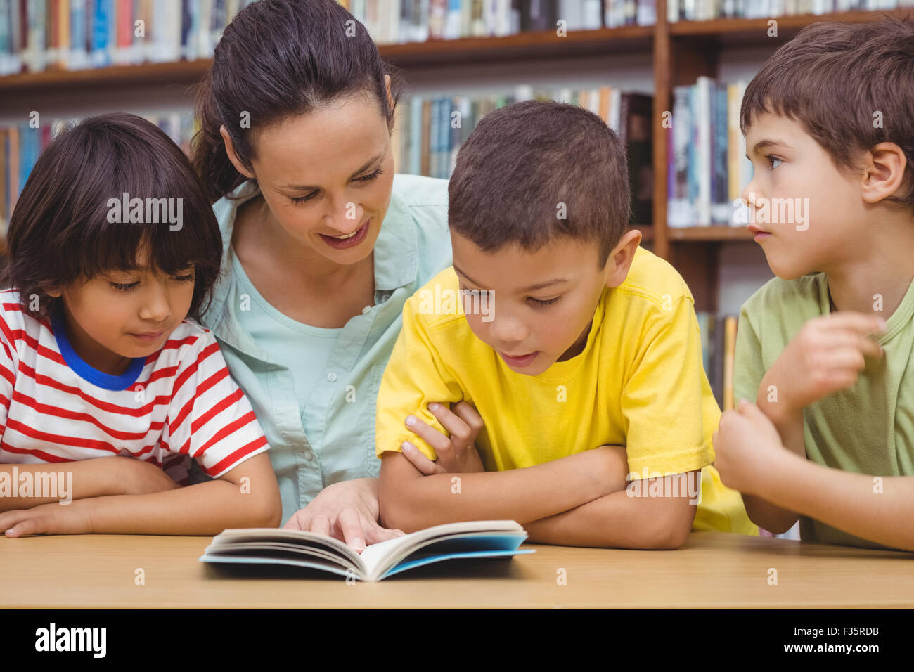 Pupils and teacher reading book in library Stock Photo - Alamy