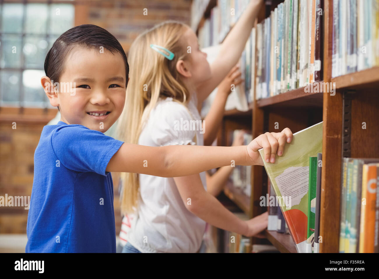 Pupils taking books from shelf in library Stock Photo - Alamy