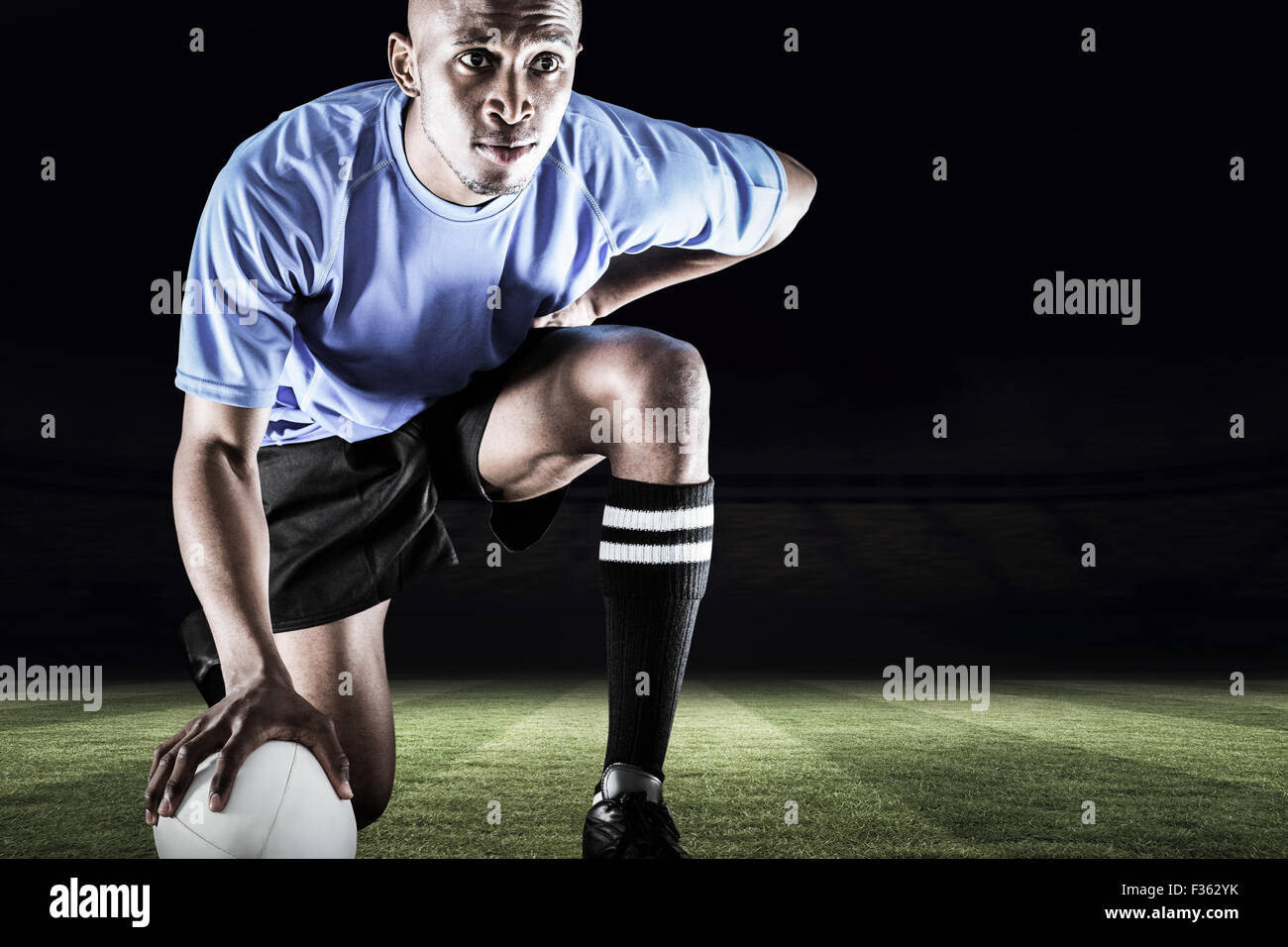 Composite image of serious rugby player kneeling while holding ball ...