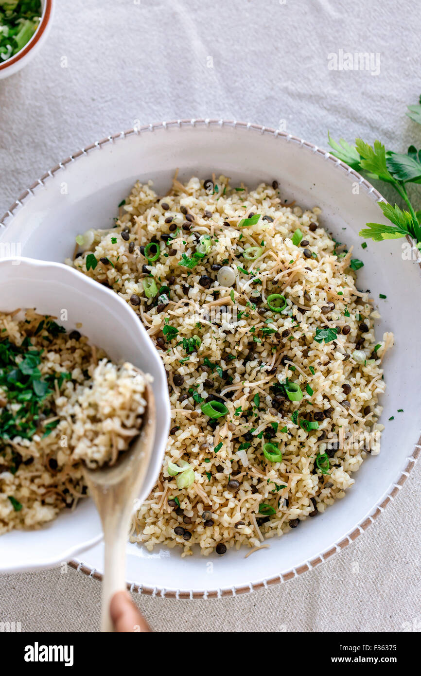 A man is filling his bowl with bulgur pilaf that is garnished with ...