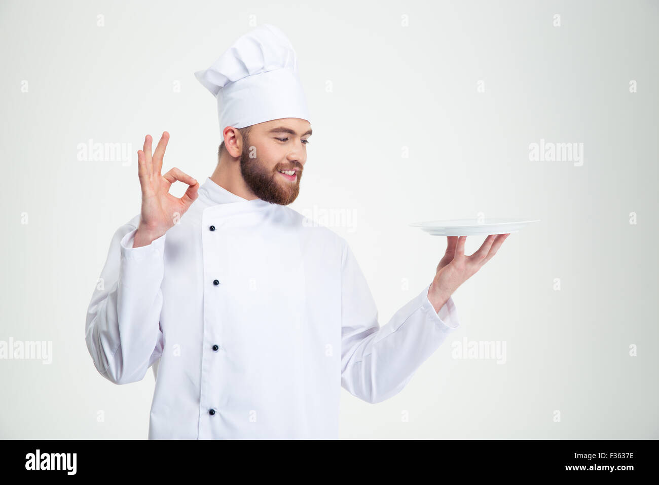 Portrait of a smiling man chef showing ok sign and empty plate isolated ...