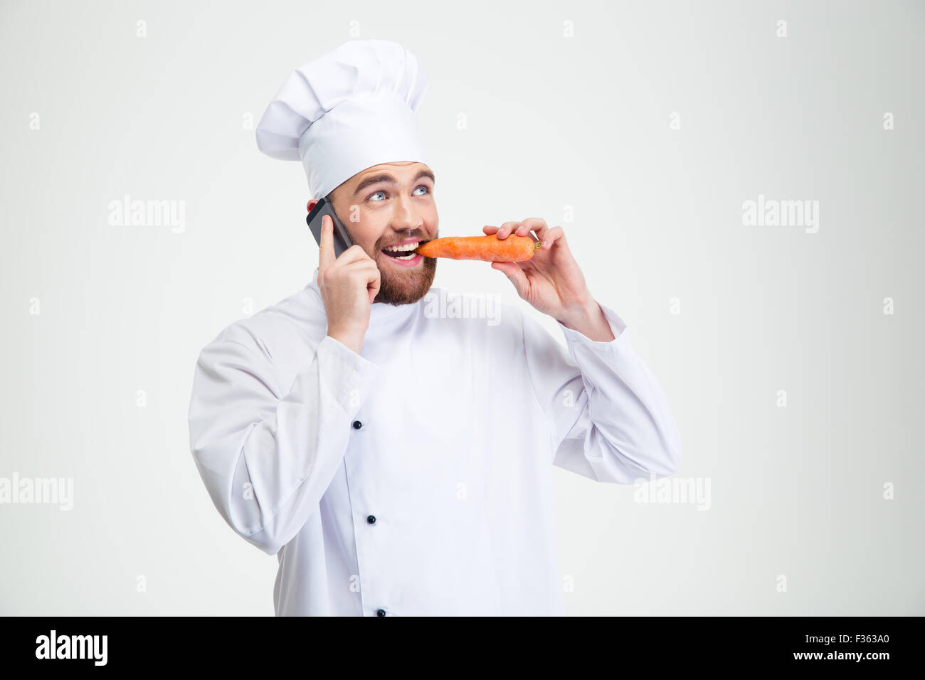 Portrait of a male chef cook talking on the phone and eating carrot ...