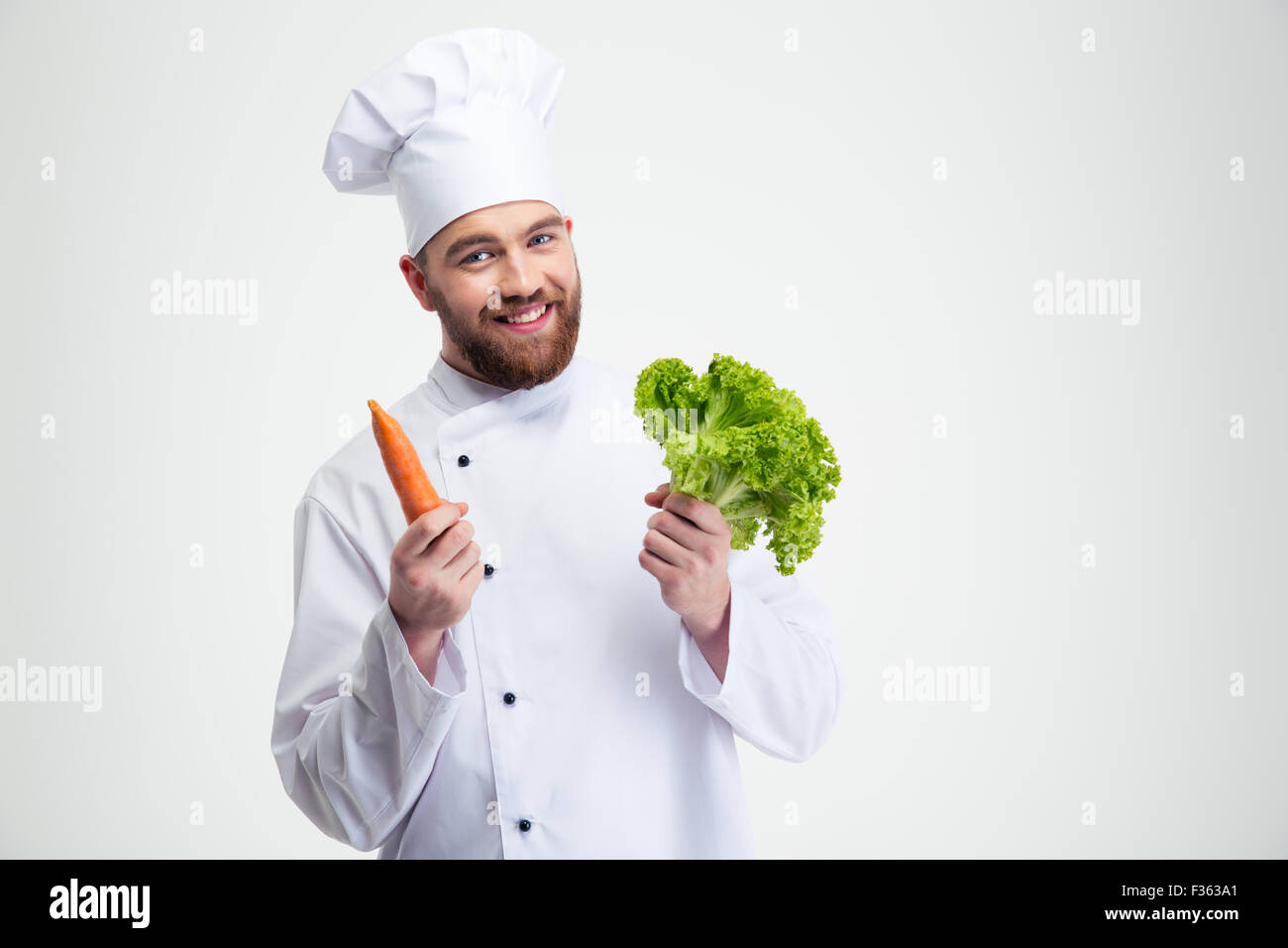 Portrait of a smiling chef cook holding salad and carrot isolated on a ...