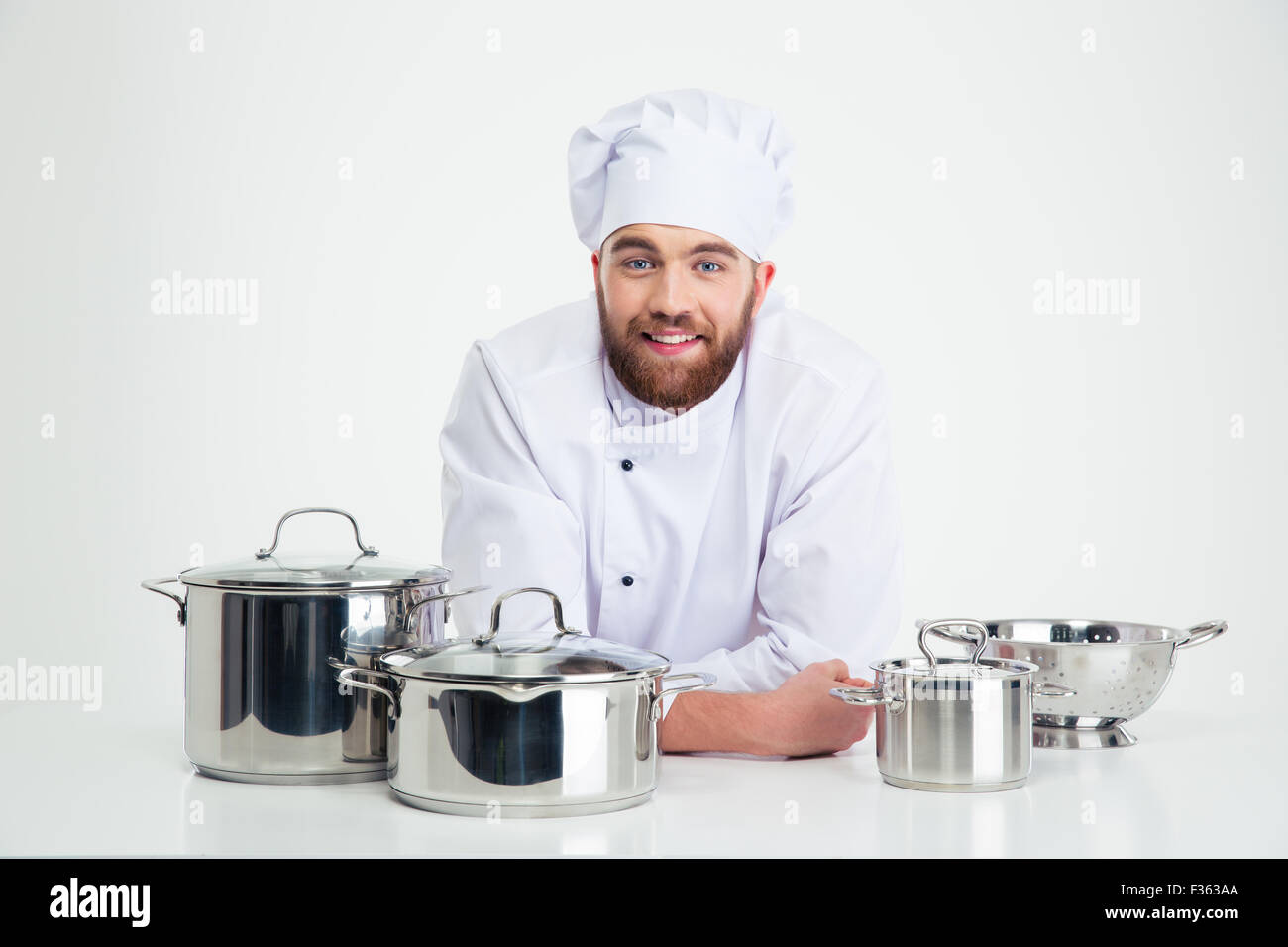 Portrait of a happy male chef cook sitting at the table with dishes ...