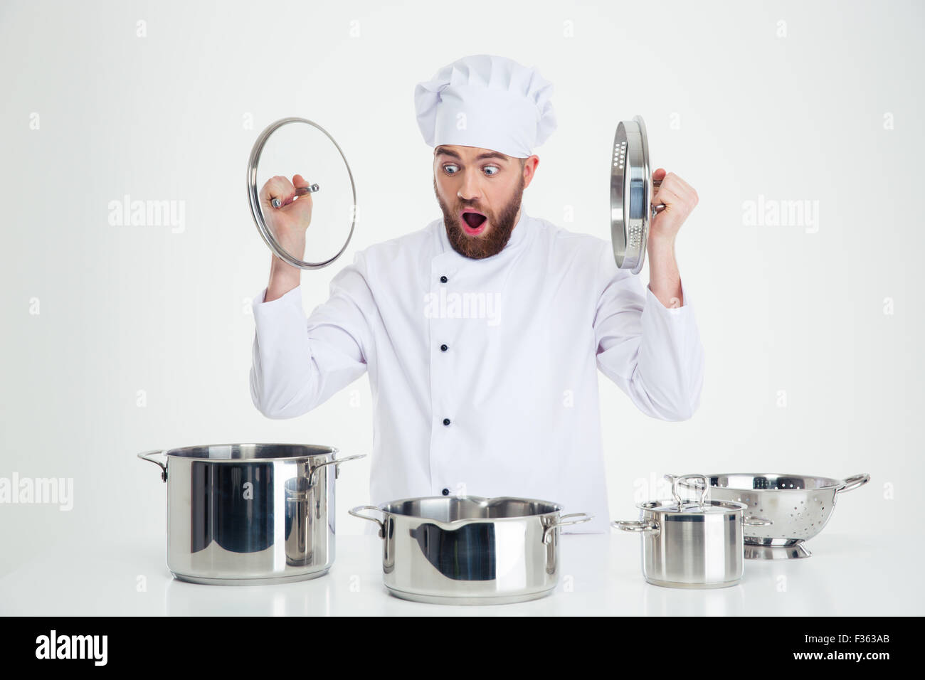 Portrait of a funny male chef cook sitting at the table with dishes ...