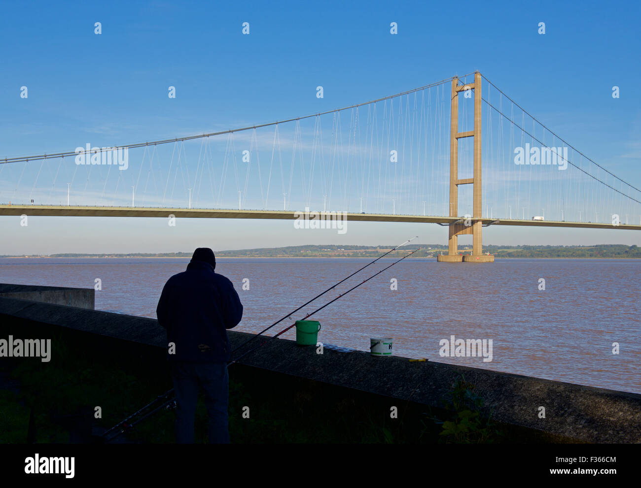 Silhouette of angler, with river Humber and Humber Bridge behind ...