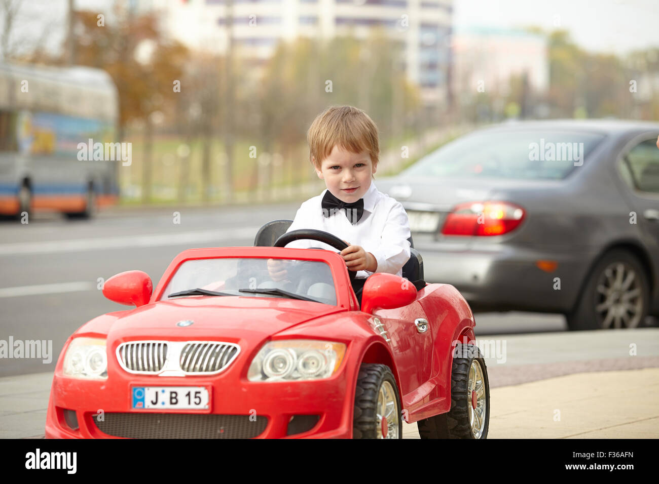 year-old boy in a white shirt in a red toy car in the street Stock ...