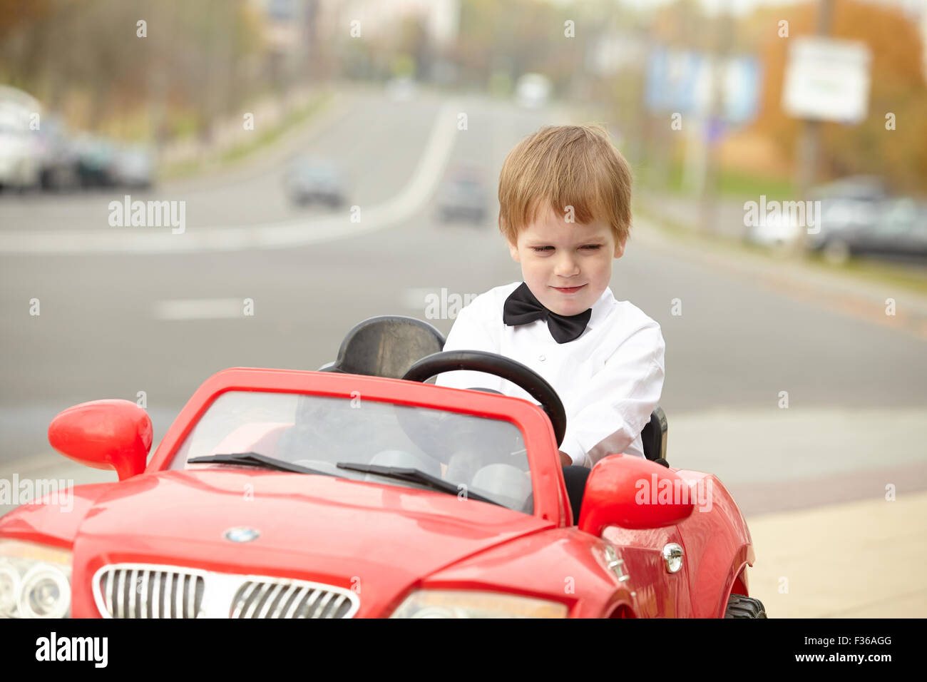 year-old boy in a white shirt in a red toy car in the street Stock ...