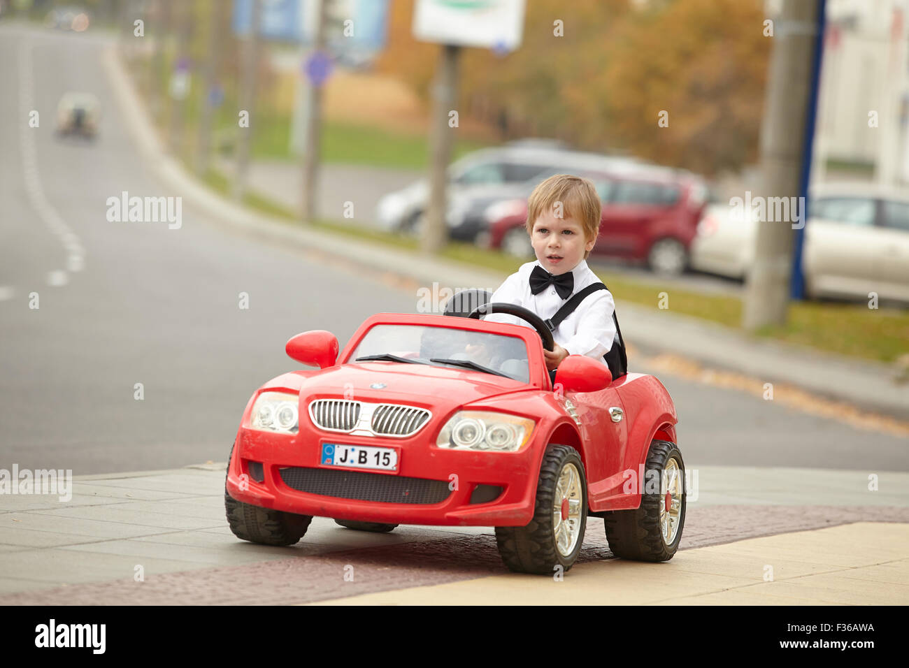 year-old boy in a white shirt in a red toy car in the street Stock ...