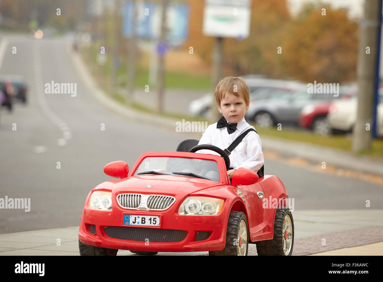 year-old boy in a white shirt in a red toy car in the street Stock ...