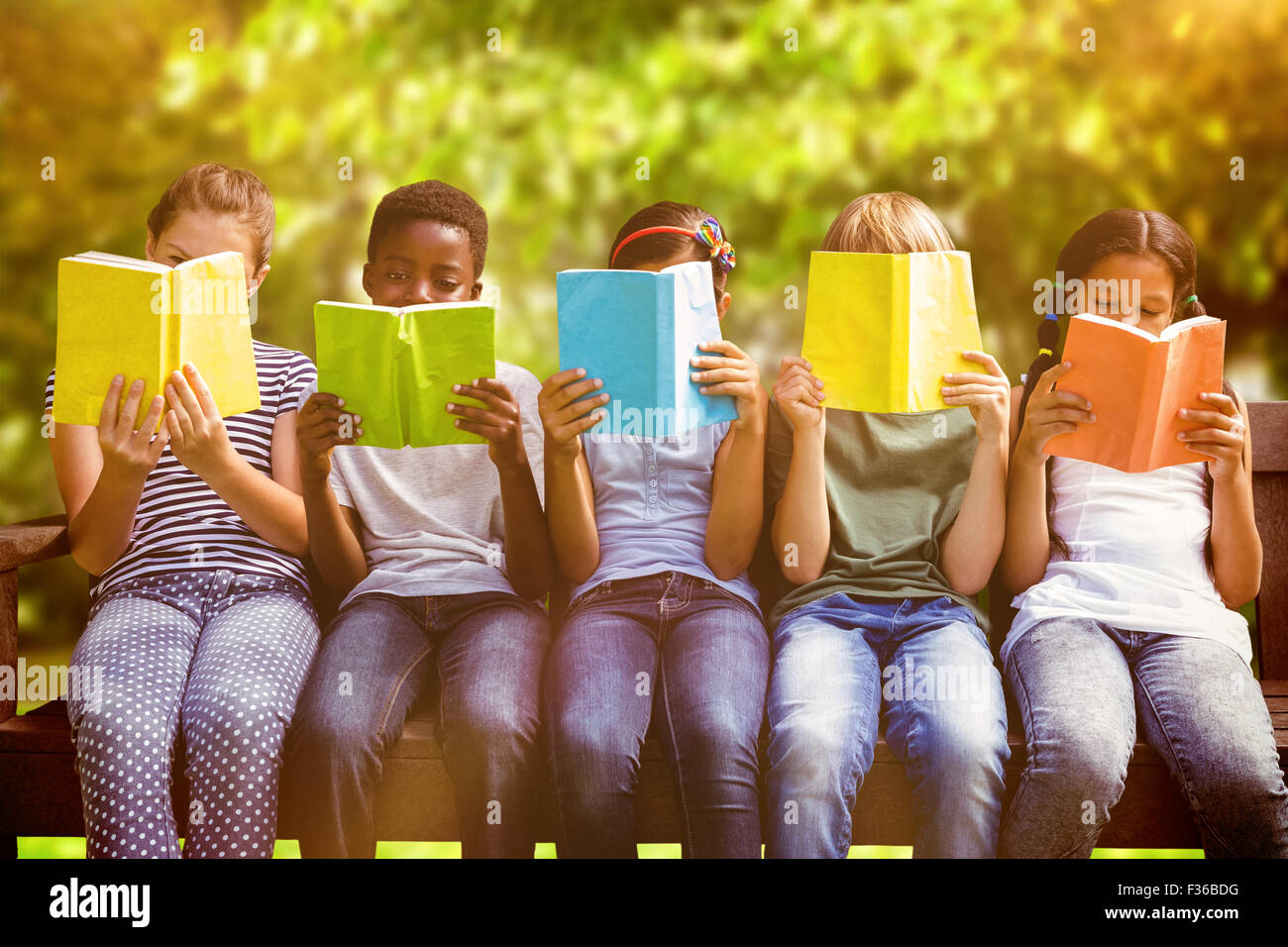 Composite image of children reading books at park Stock Photo - Alamy