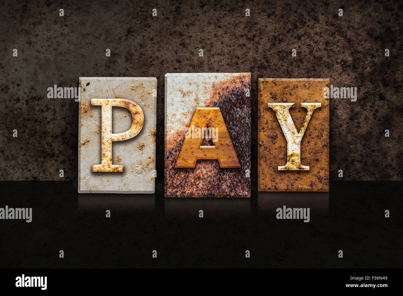 The word "PAY" written in rusty metal letterpress type on a dark ...