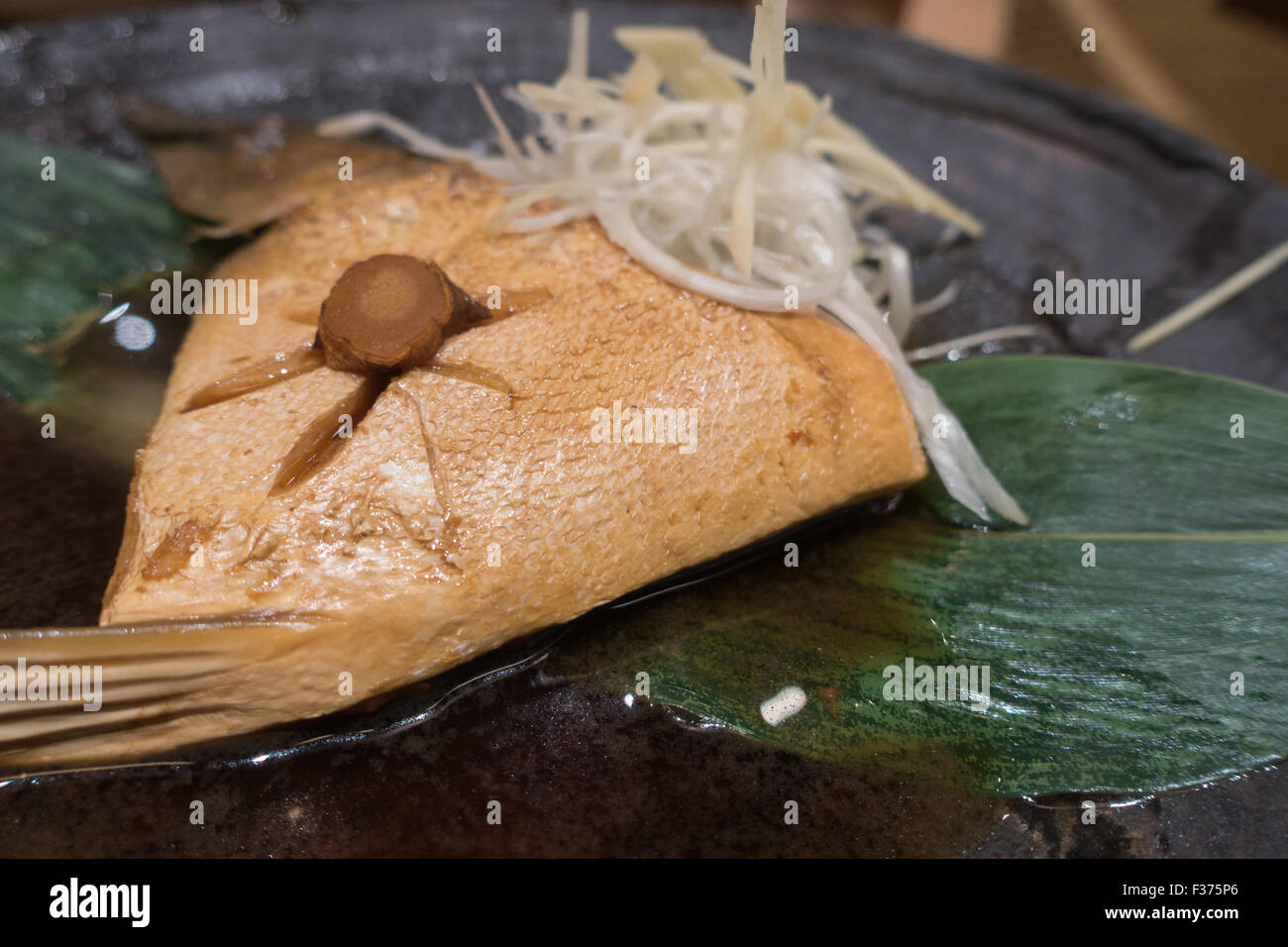 Hamachi cooked in sauce on black ceramic plate Stock Photo - Alamy