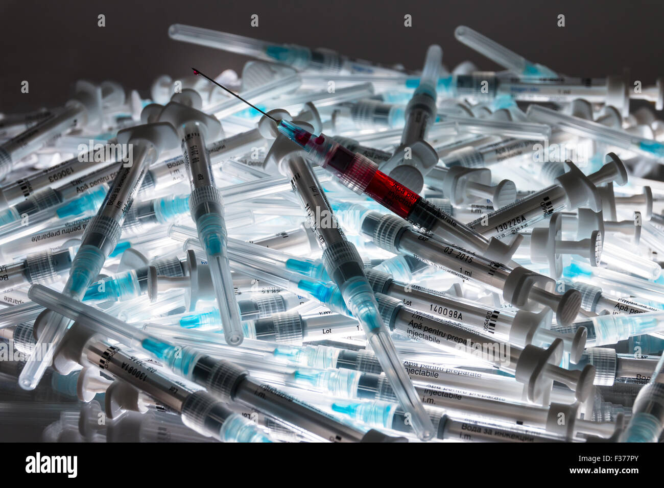 A bunch of used syringes, lit from below, with one syringe containing ...
