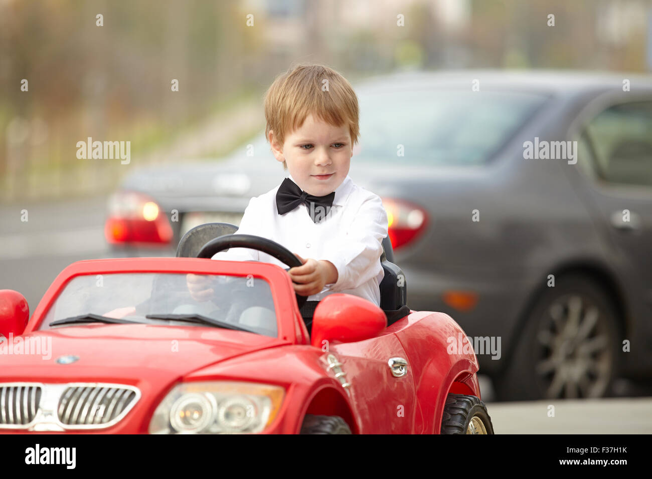 year-old boy in a white shirt in a red toy car in the street Stock ...