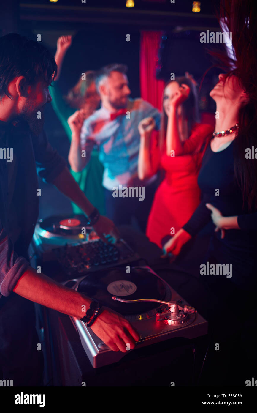 Modern deejay adjusting sound on turntables and looking at dancing ...