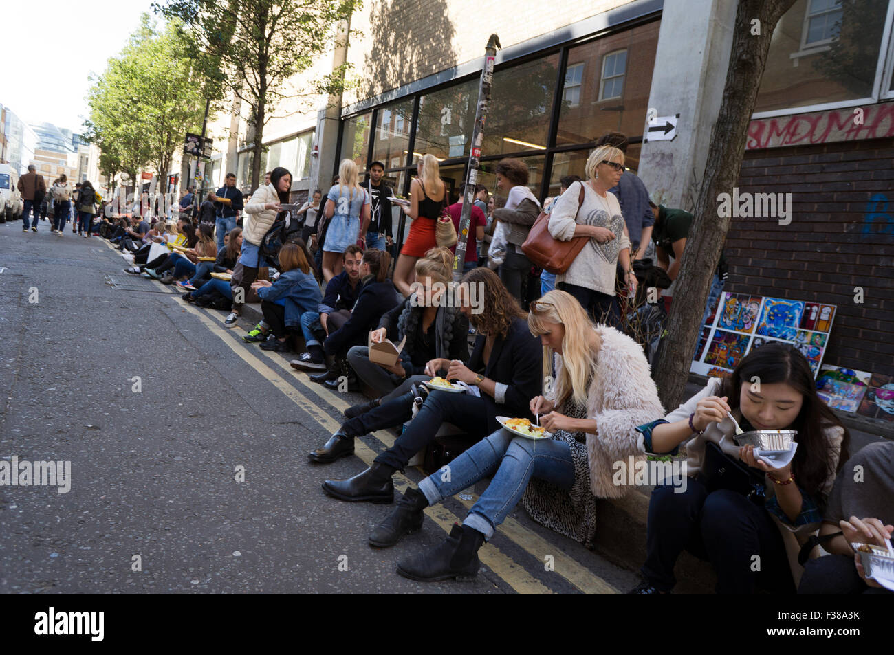 People eating street food sitting on the pavement, brick lane, London ...