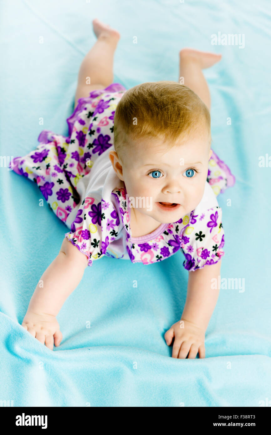 blue-eyed baby girl in a dress creeps on the blue coverlet Stock Photo ...