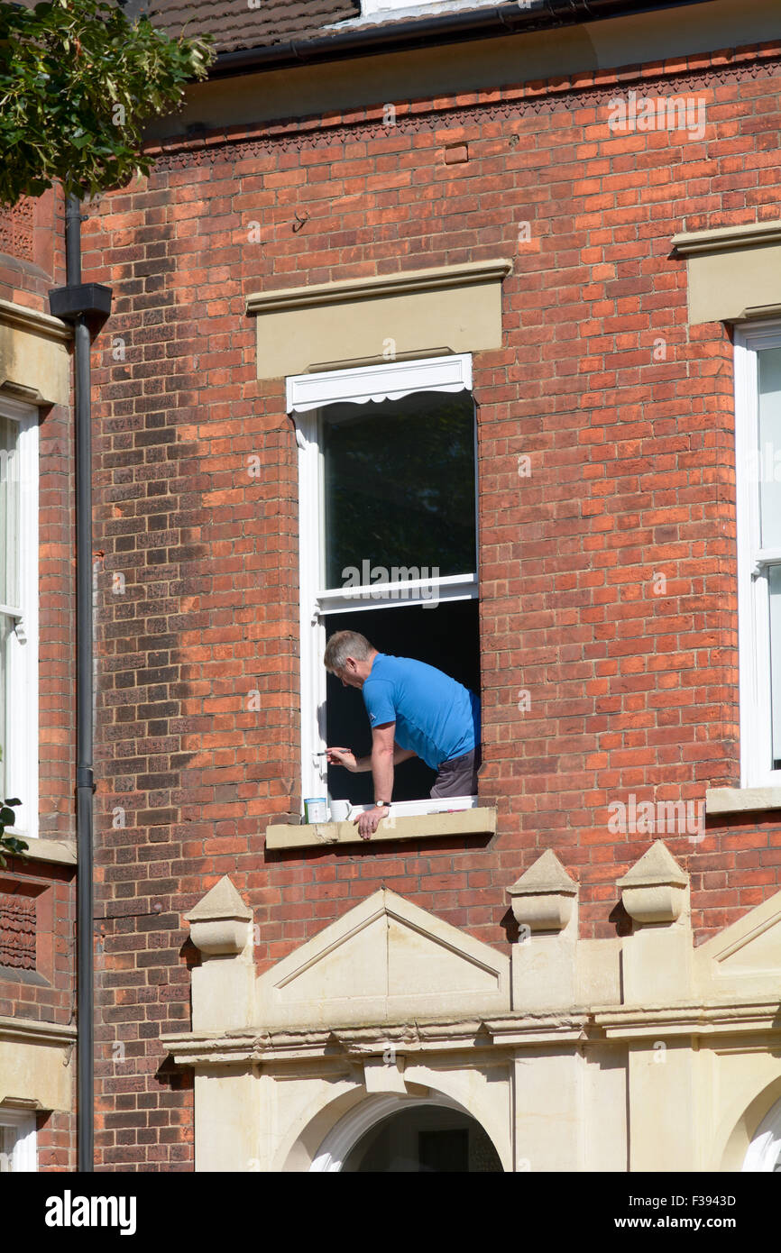 Man leaning out of first floor window of house painting wooden window ...
