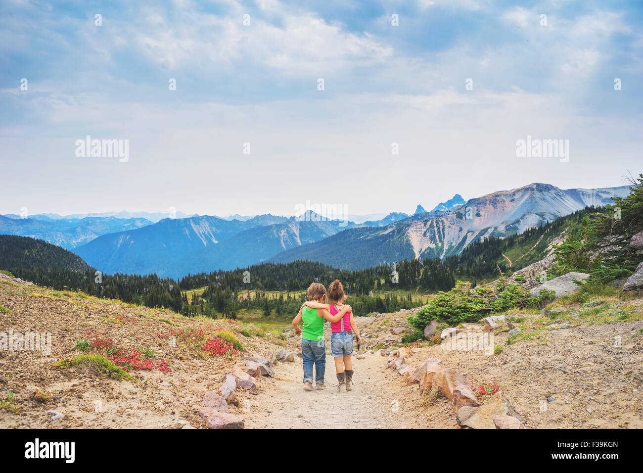 Rear view of Boy and girl walking along a path with their arms around ...