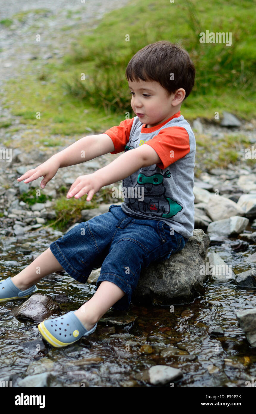 A young boy sits on a boulder in the middle of a stream Stock Photo - Alamy