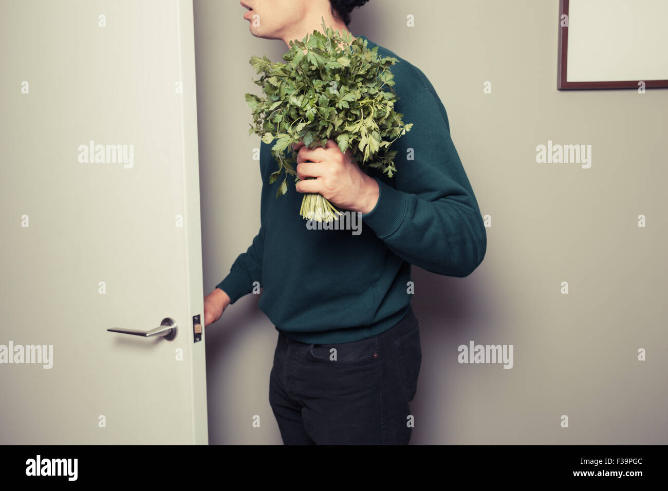 A surprised young man holding a bunch of parsley is answering the door ...
