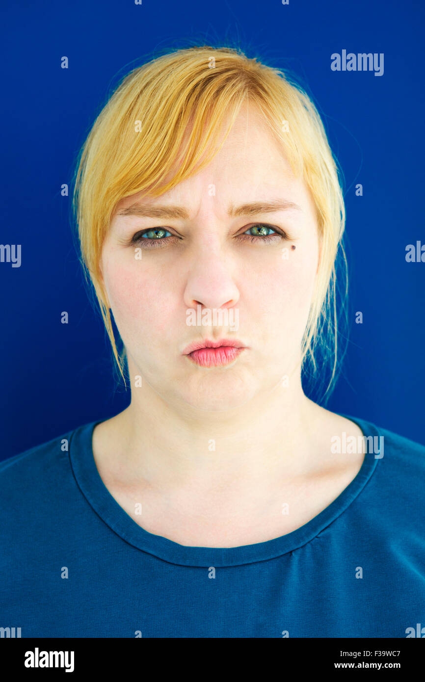 portrait of young blond woman looking angry with blue background Stock ...
