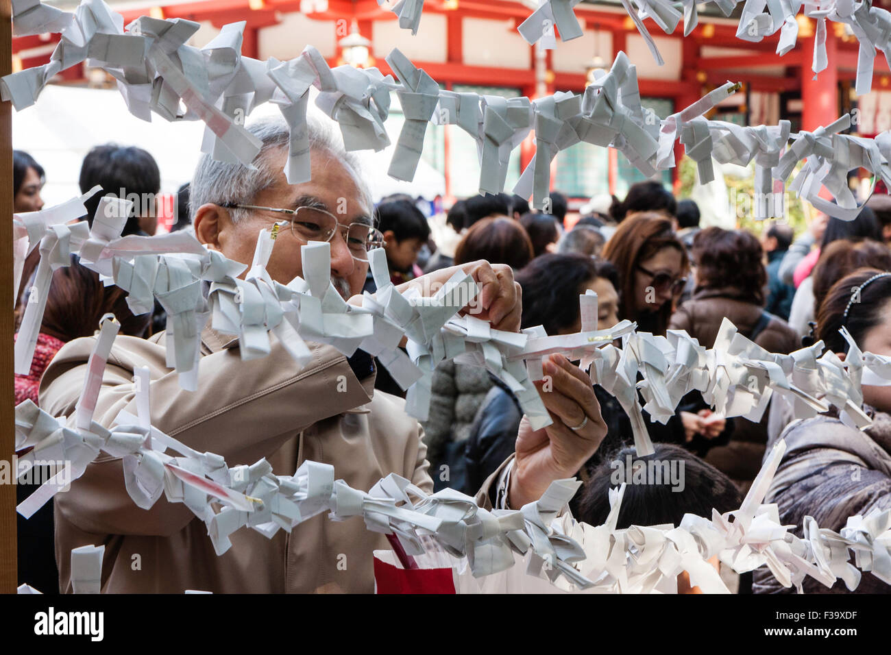 Mature Japanese man tying his 'bad luck' fortune paper slip, omikuji ...