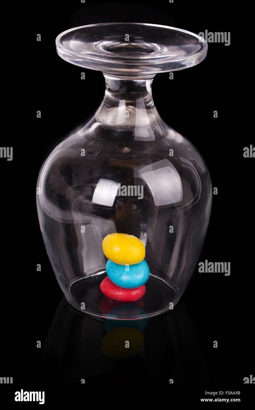Inverted glass and three colored stones isolated on black background ...