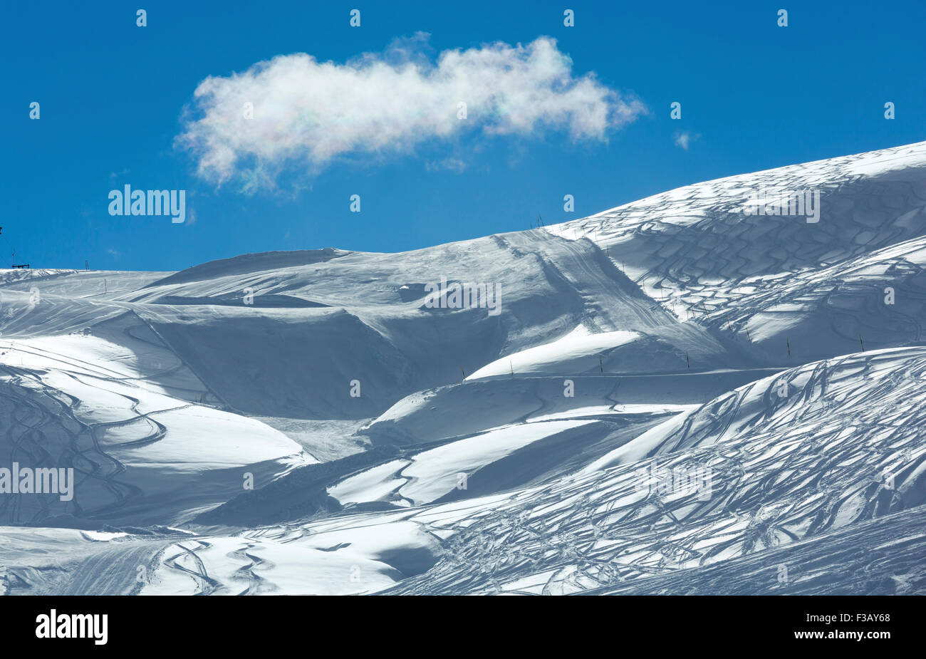 Hillside freaked ski tracks and lonely cloud in the blue sky. Winter ...