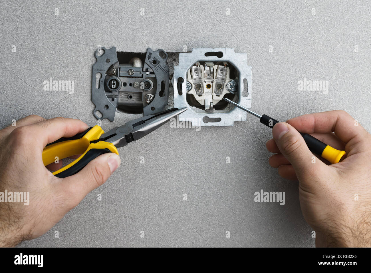 Installing a wall-mounted AC power socket with a screwdriver on a grey ...