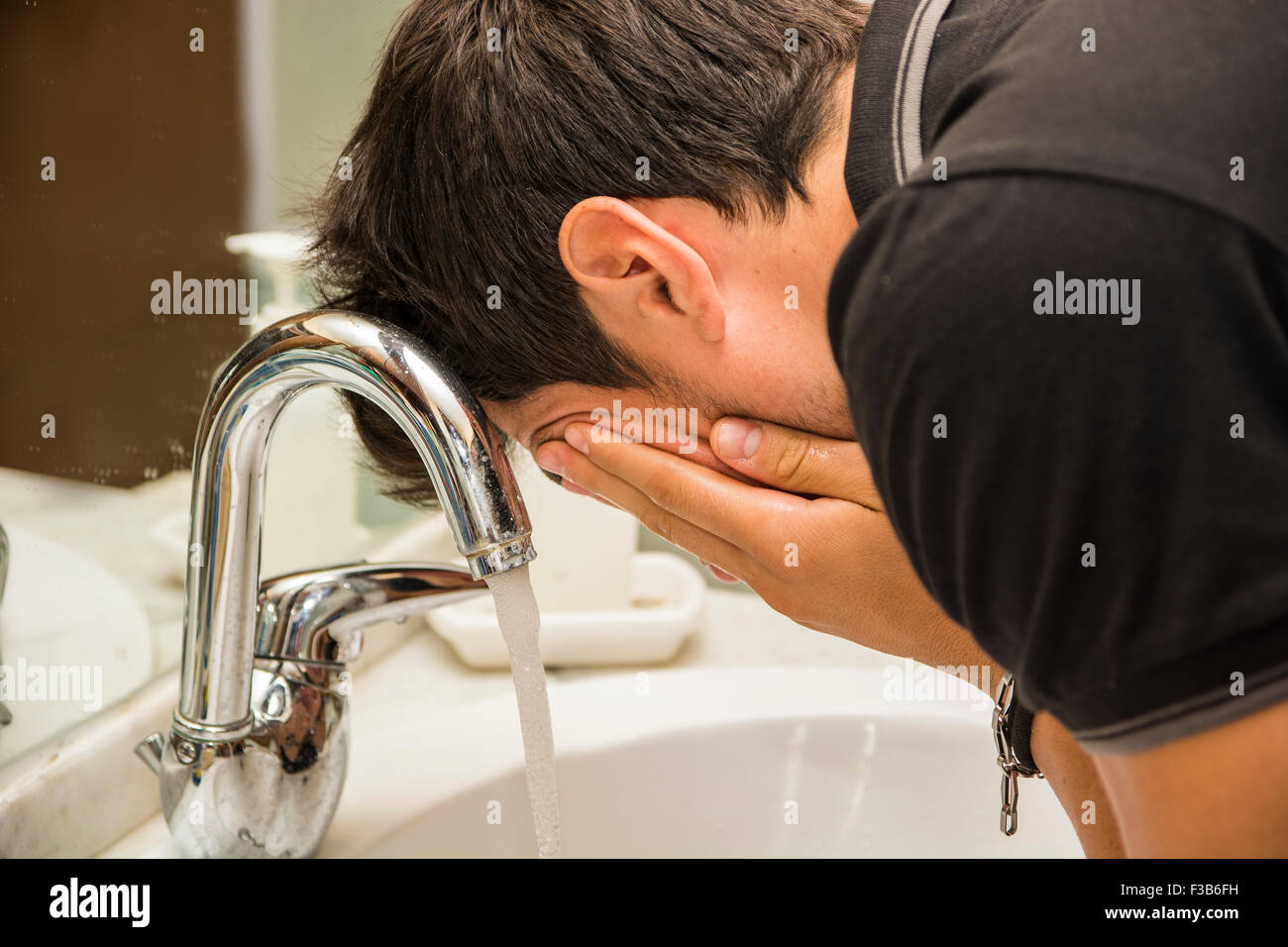Attractive young man washing his face, splashing water on himself over ...