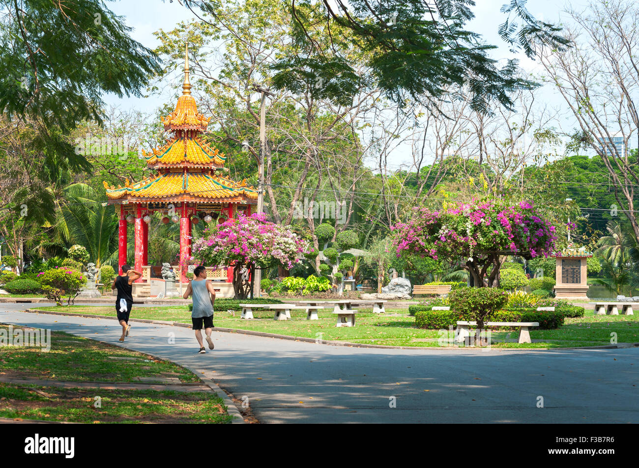 Two male runners run past the Chinese pavilion in Lumpini Park, Bangkok ...