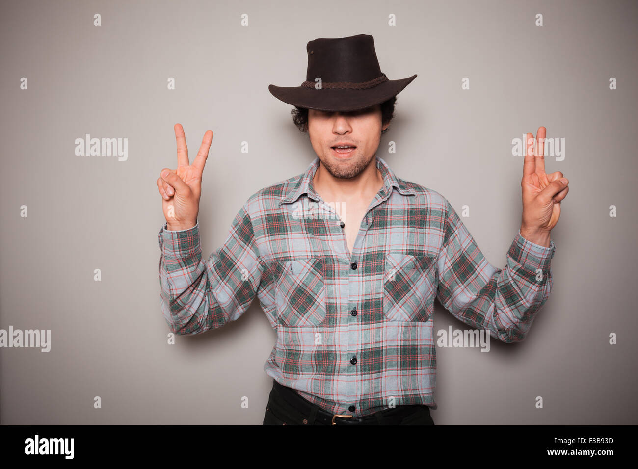 A young cowboy wearing a plaid shirt is posing against a green wall ...