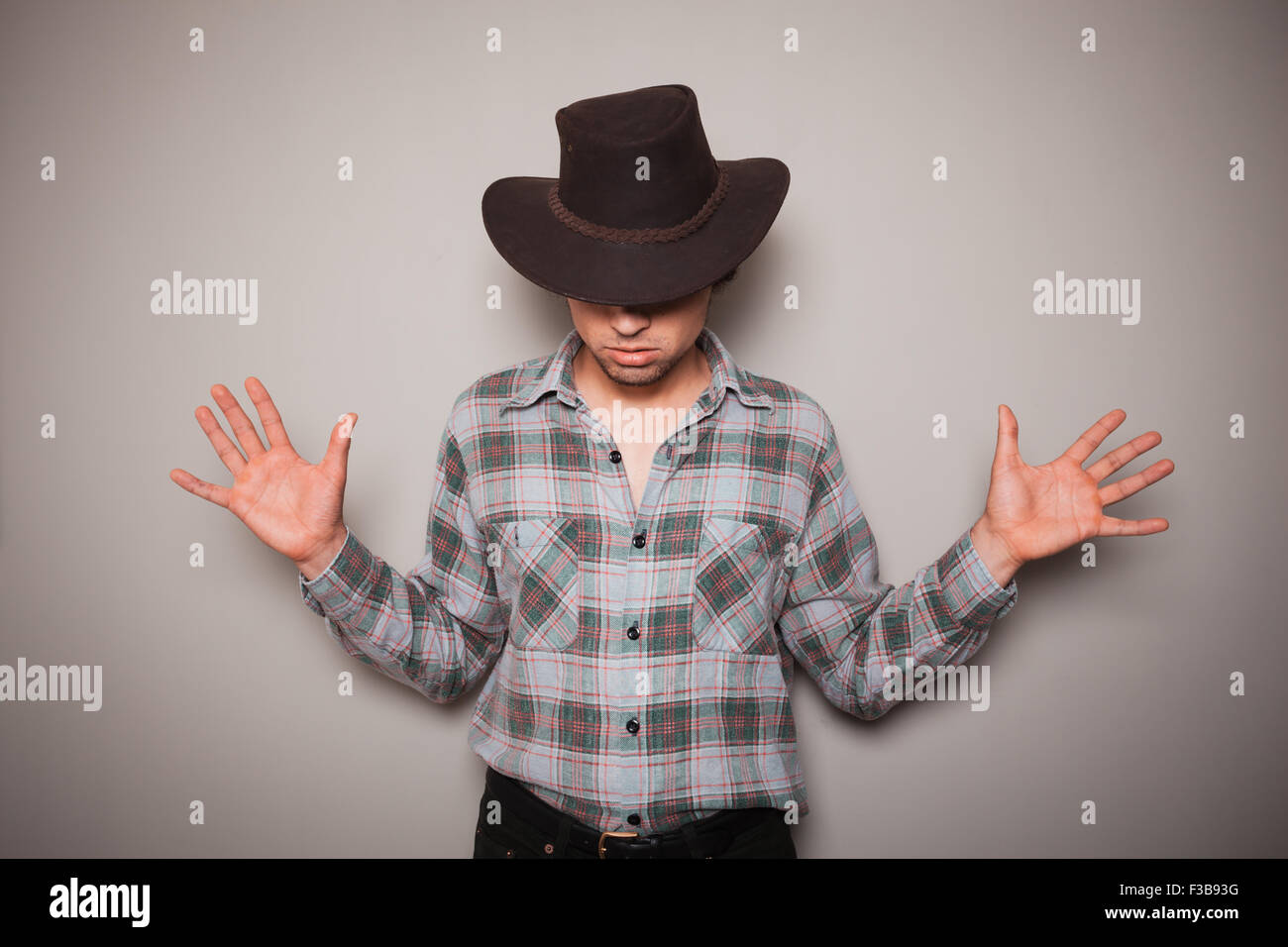 A young cowboy wearing a plaid shirt is posing against a green wall ...