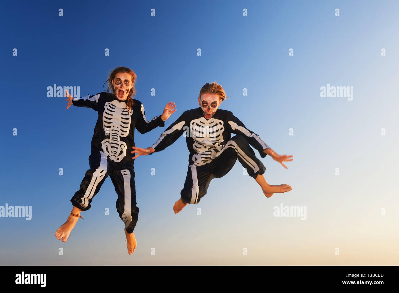 Two young girls in scary skeleton costumes jumping high in the air with ...