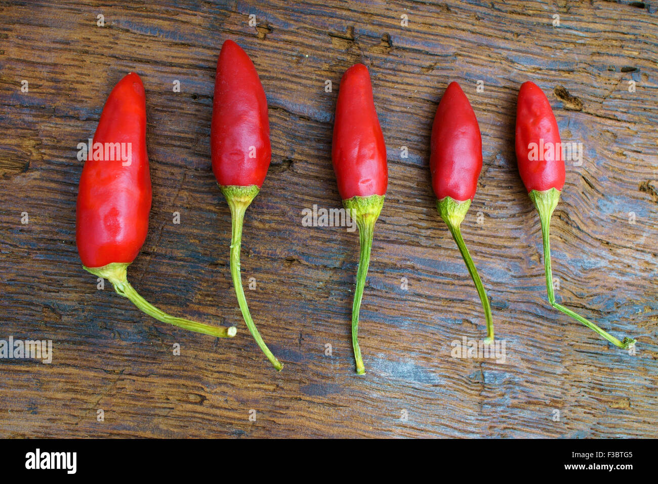 Five whole red chili pepper pods on an old rustic wooden table Stock ...