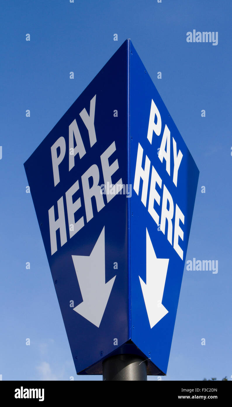 A 'Pay Here' sign in a parking lot with ticket cash machines ...