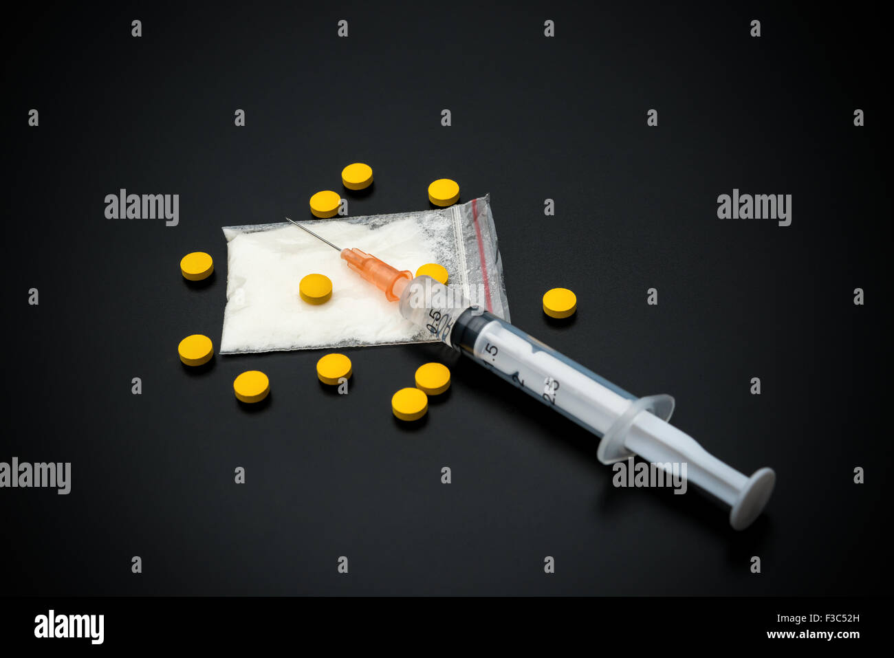 disposable syringe and pack of white powder and pills on black ...