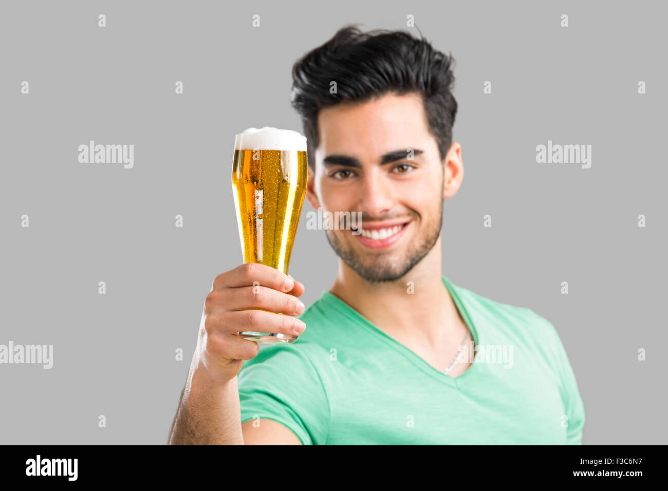 Portrait of handsome young man tasting a draft beer, isolated on gray ...