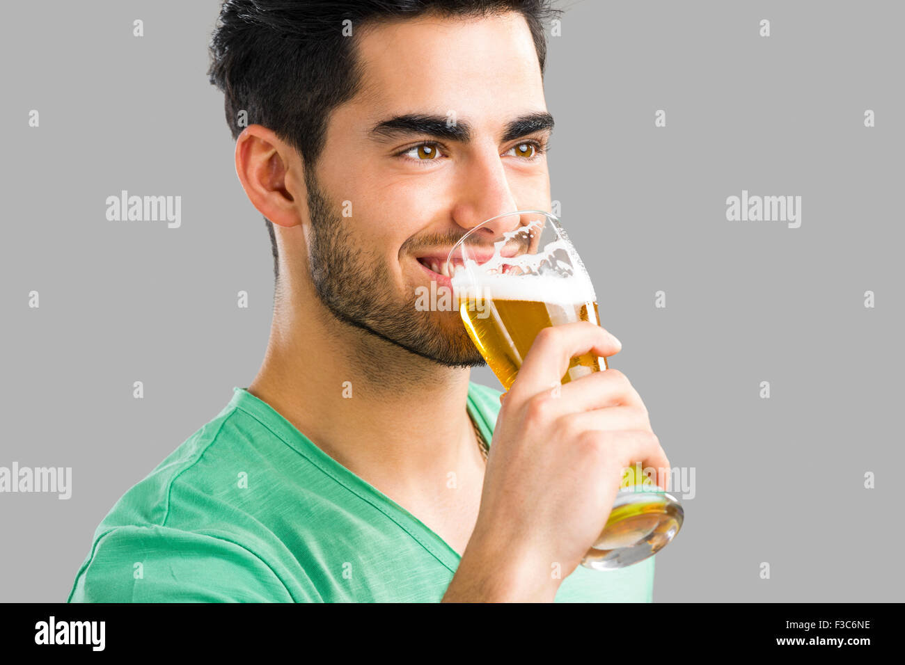 Portrait of handsome young man tasting a draft beer, isolated on gray ...