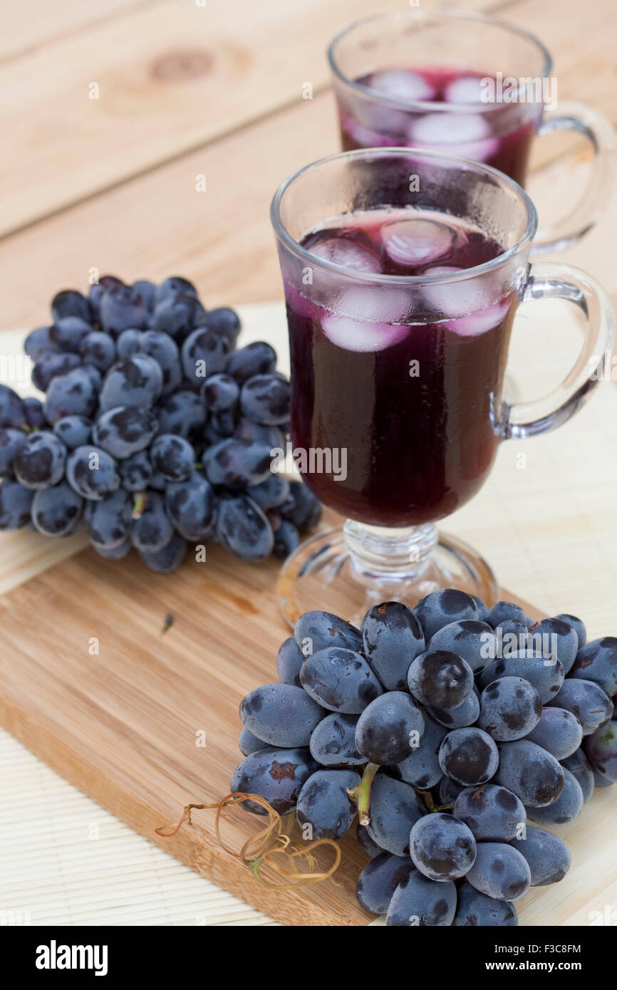 Grape juice cooler with ice in glass and glass of fresh blue grapes on ...