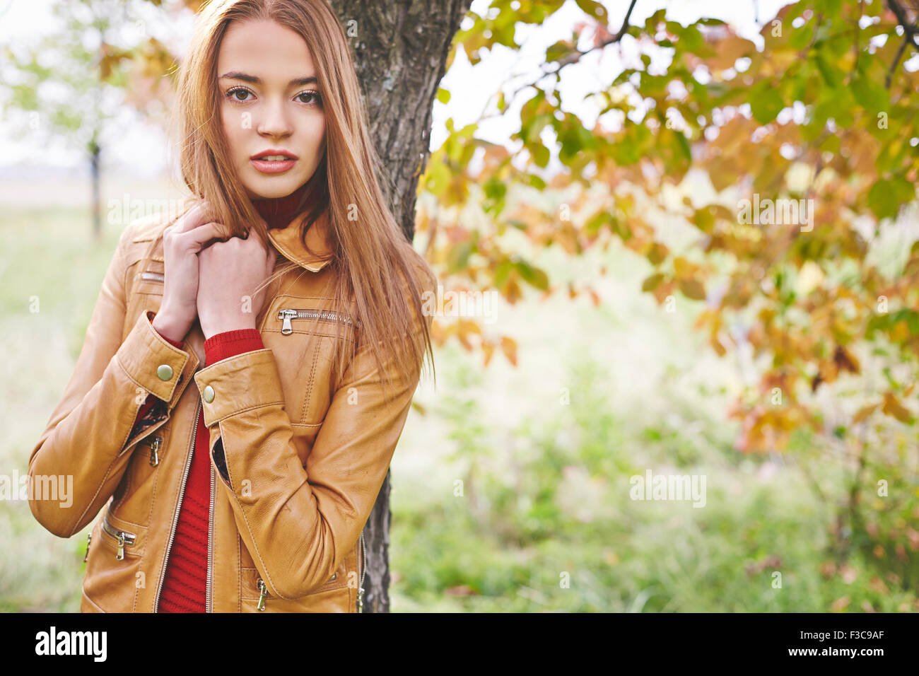 Pretty young woman in leather jacket looking at camera while standing ...