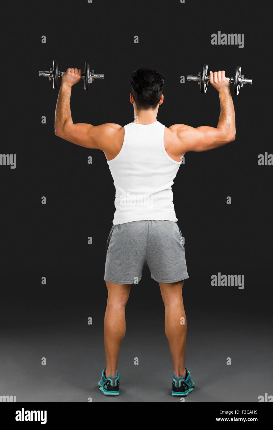 Portrait of handsome young man lifting weights, isolated over a gray ...