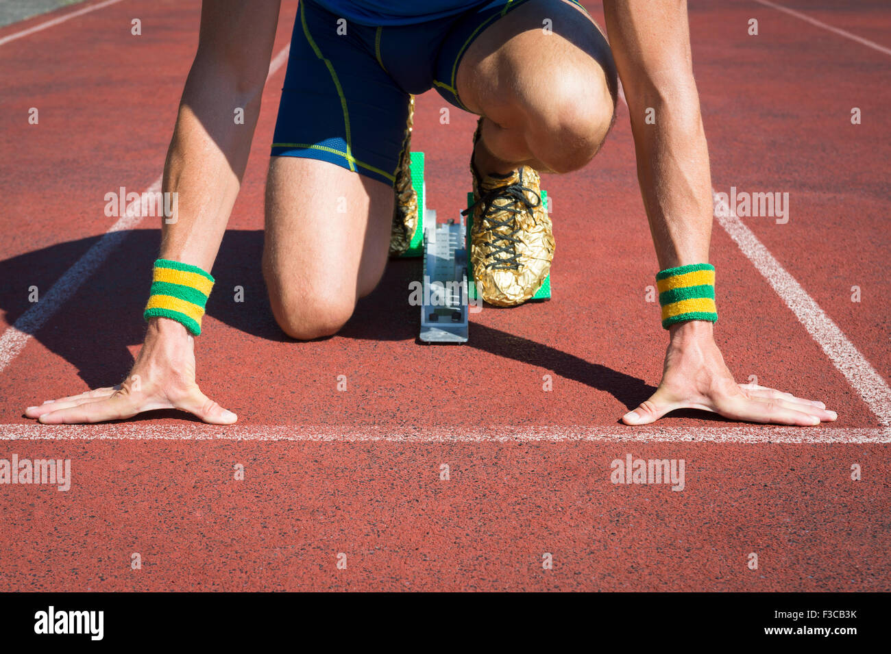 Athlete crouching at the starting line of a running track with gold ...