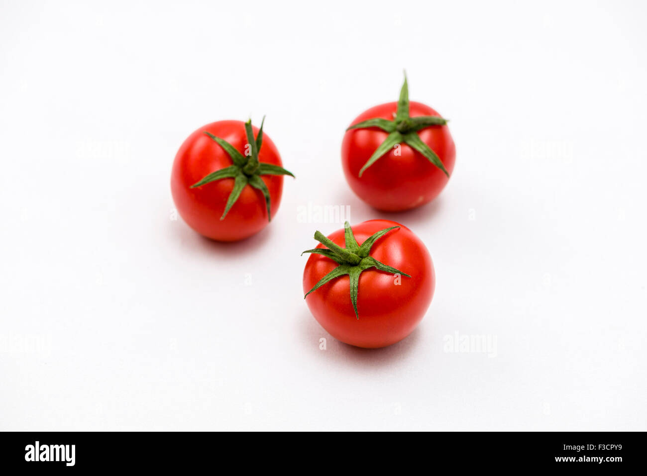 Three red tomatoes (Solanum lycopersicum), displayed on white table ...