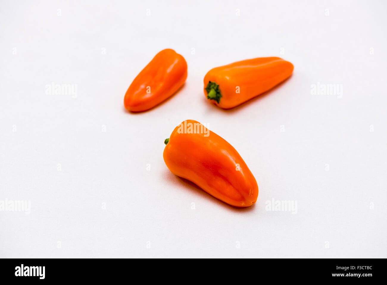 Three orange capsicums (Capsicum annuum), displayed on white table ...