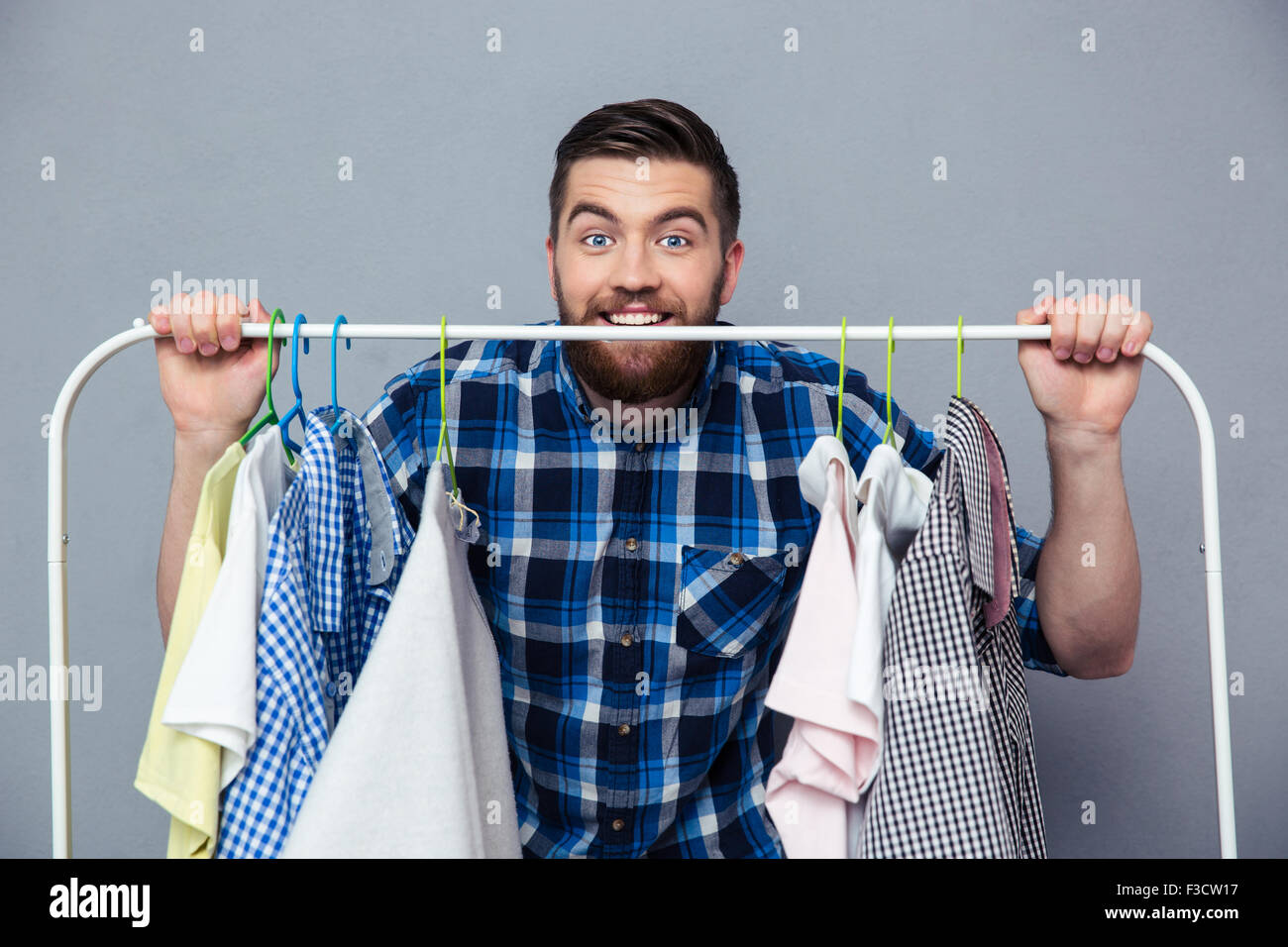 Portrait of a happy hipster man standing with rack of clothes on gray ...