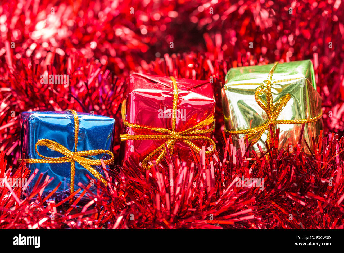 Three gift boxes on red tinsel, close-up view Stock Photo - Alamy
